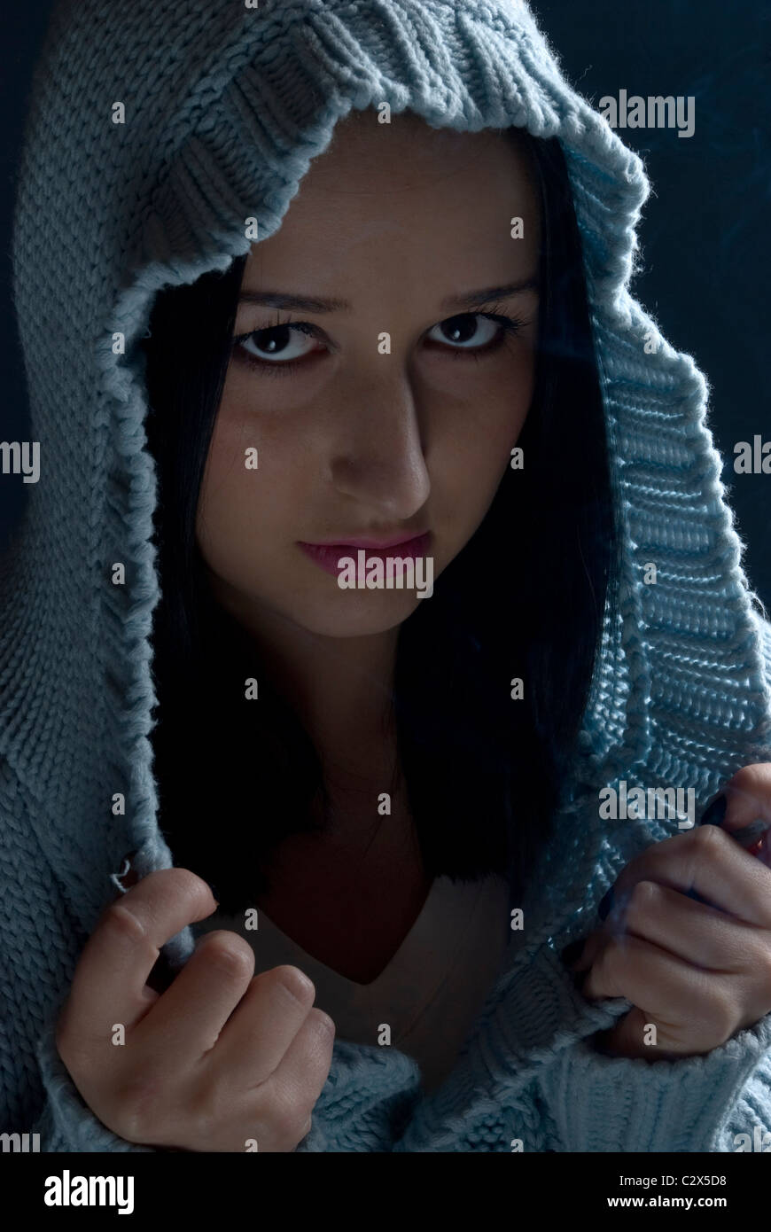 Portrait of girl with evil look wearing wool hood in darkness with ...