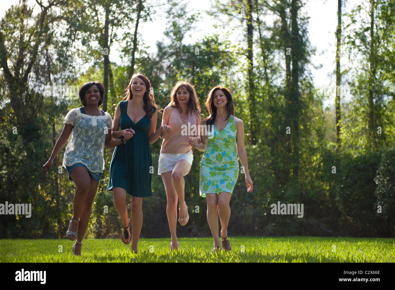 Four young women in 30s skipping arm in arm across a field laughing ...