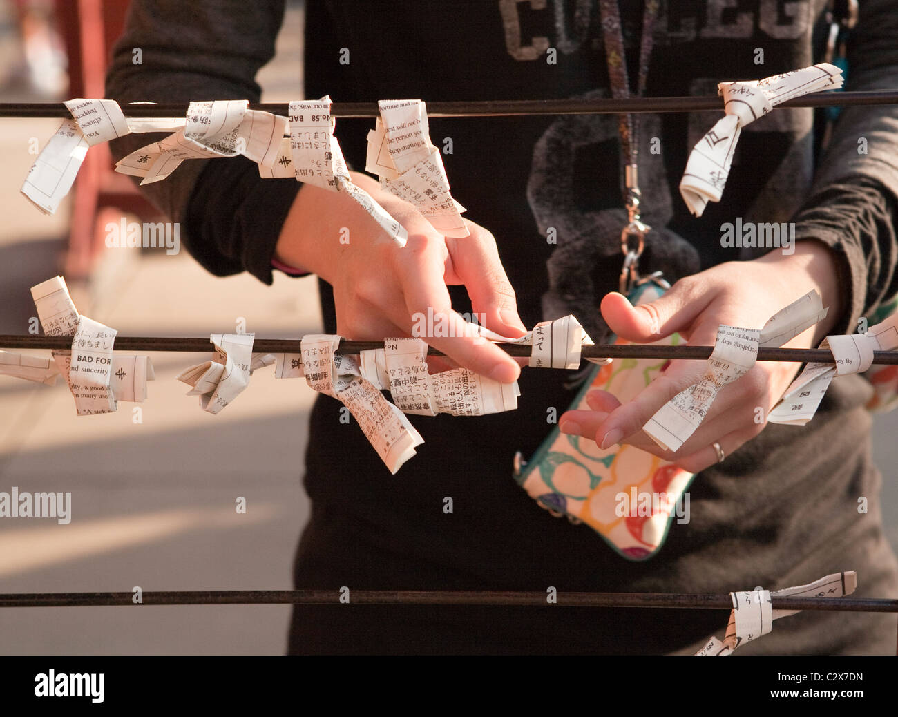A PERSON TIDYING A FORTUNE PAPER STRIP TO A WIRE RACK AT SENSO-JI ...