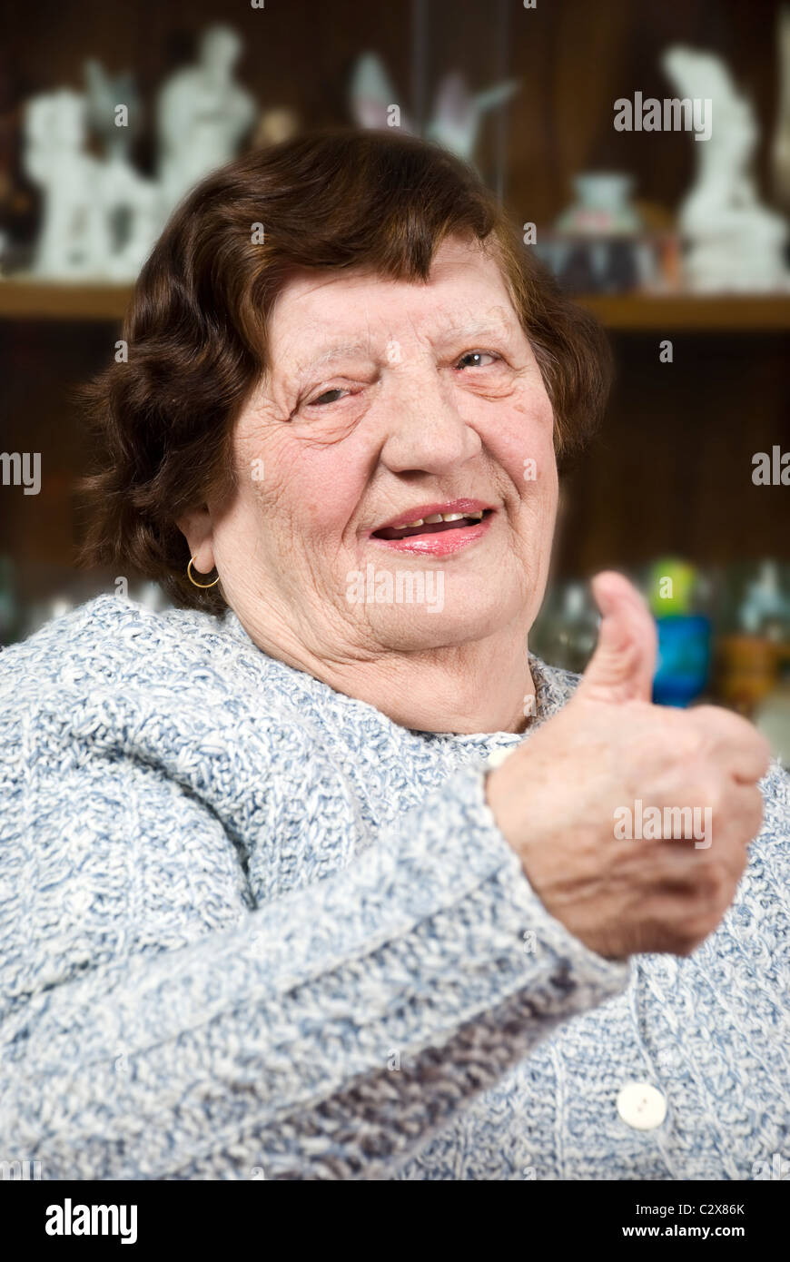 Portrait of elderly woman giving thumbs up and smiling in her living ...