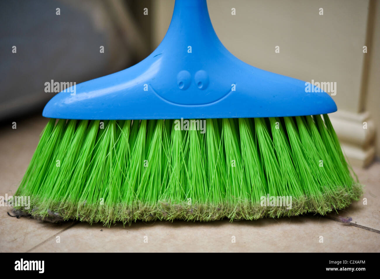 Smiling face on a bright blue and green kitchen broom on a beige tiled ...