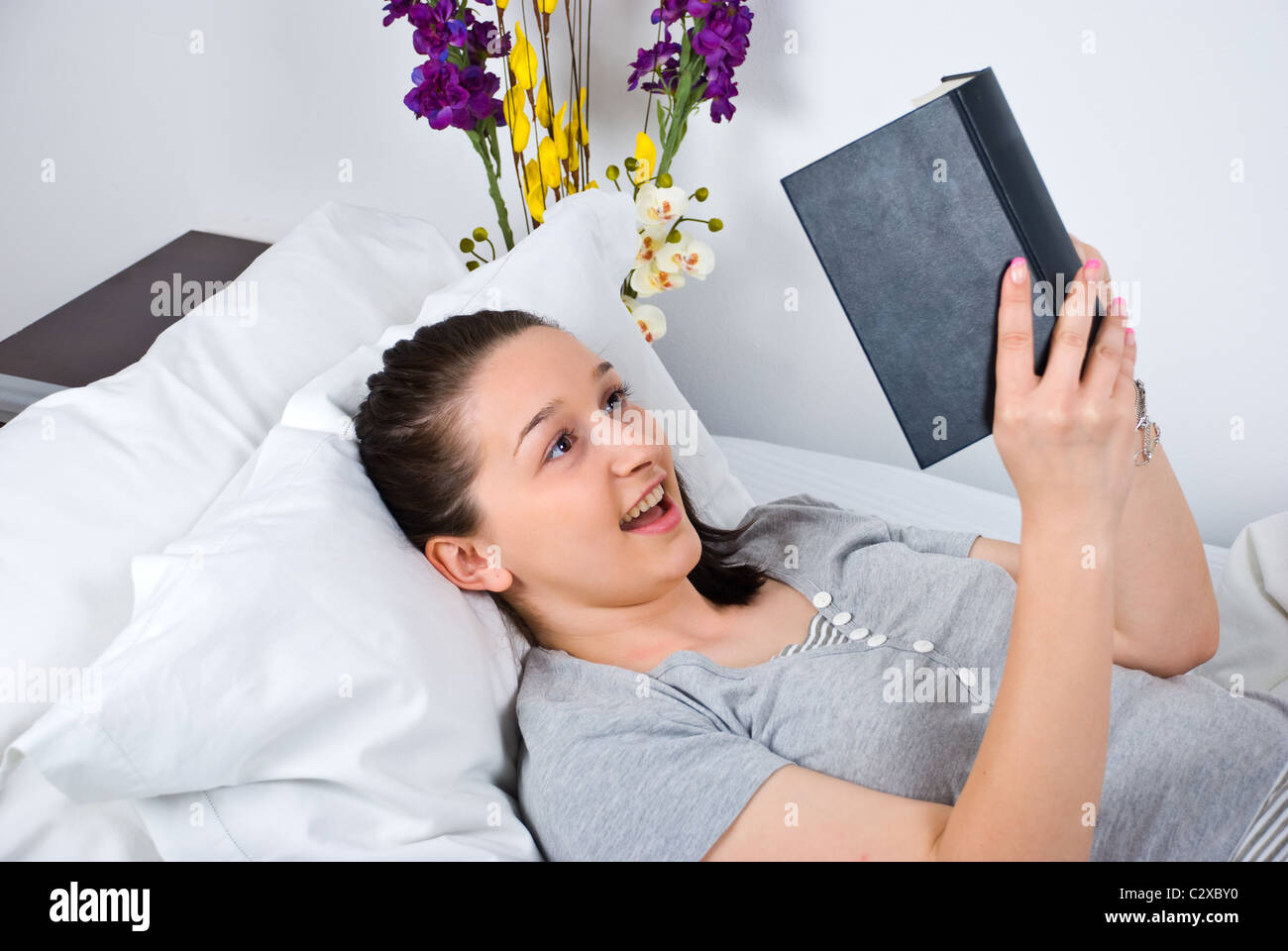 Woman lying on bed reading a captivate book and looking surprised Stock ...