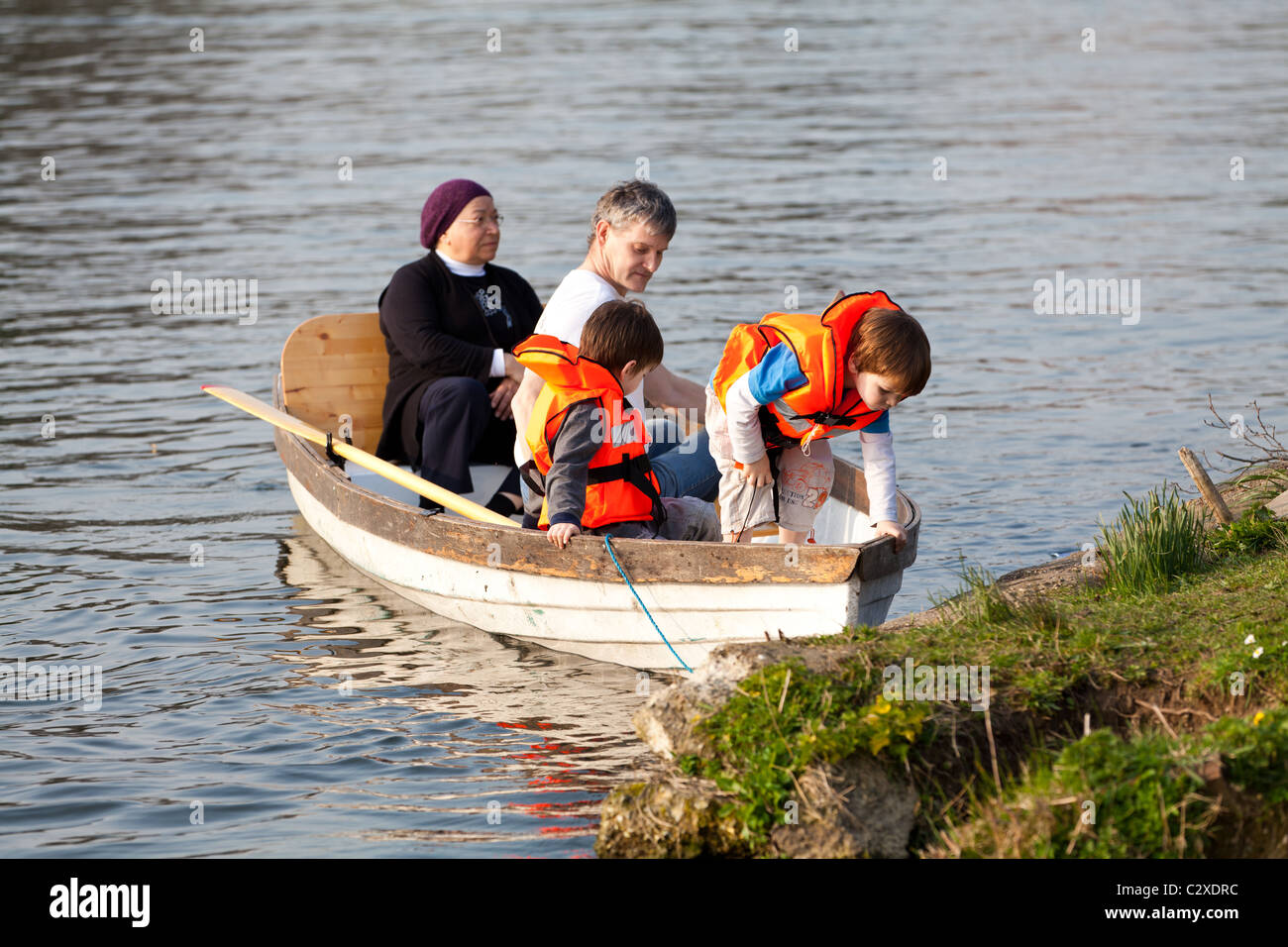 Family in a boat reaching the riverbank. Children wearing brightly ...