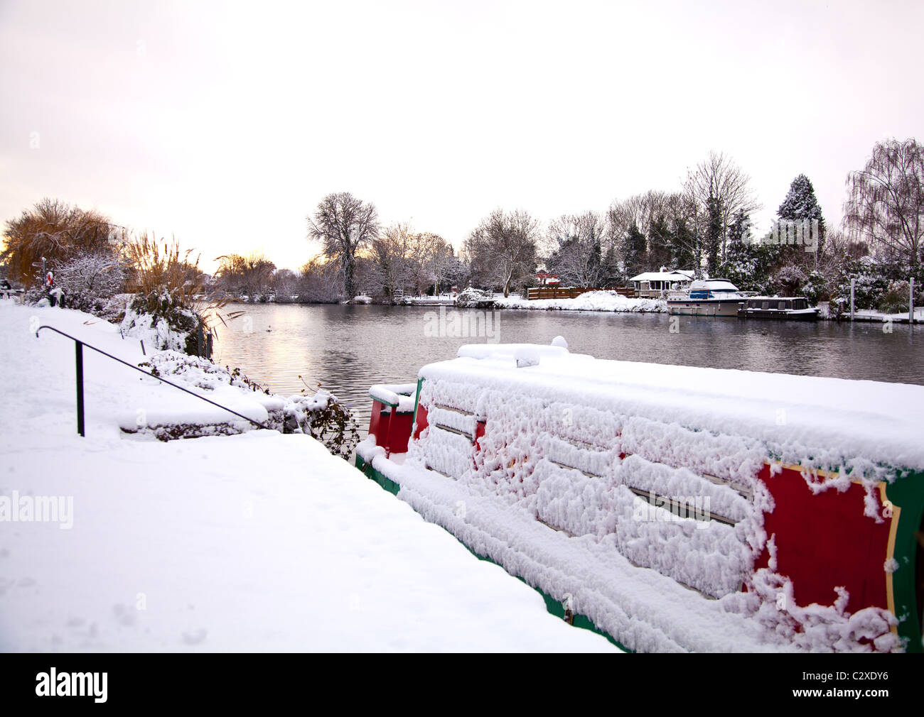 Sun going down and a red barge docked by the river side covered in snow ...