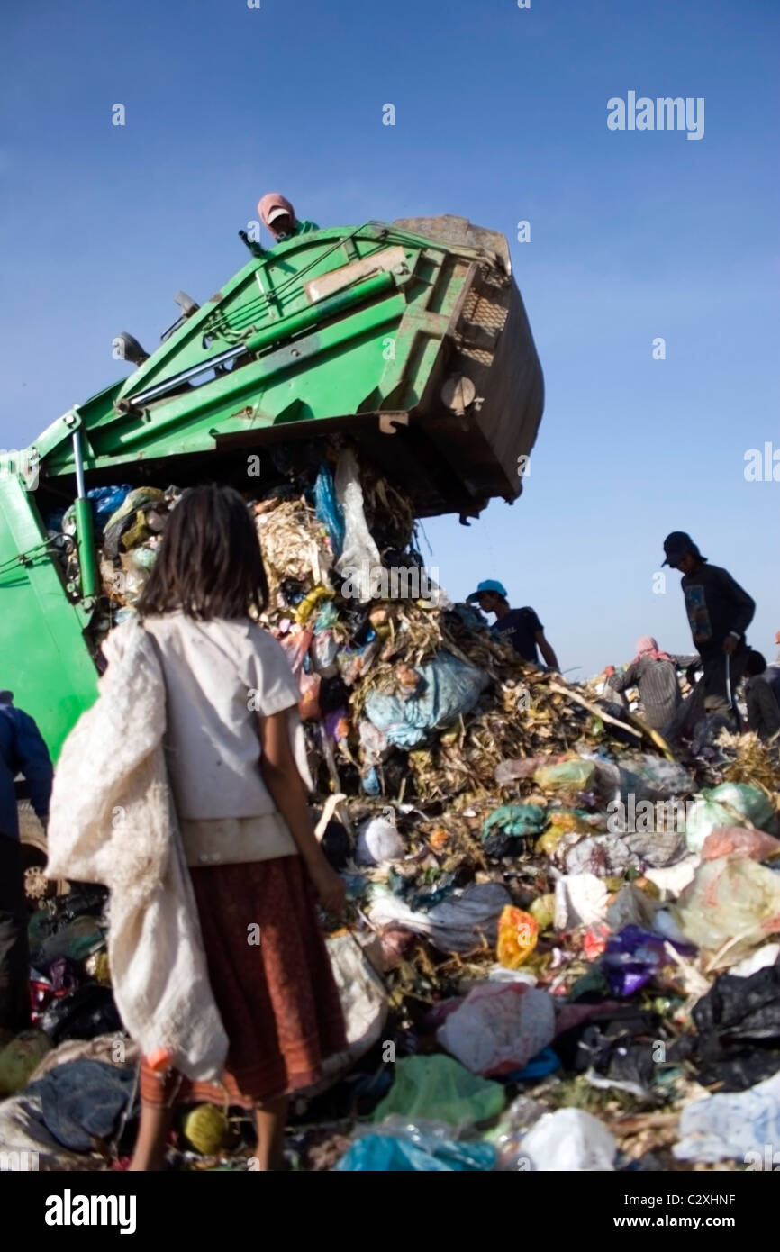 A child laborer girl is standing near a garbage truck at a toxic and ...