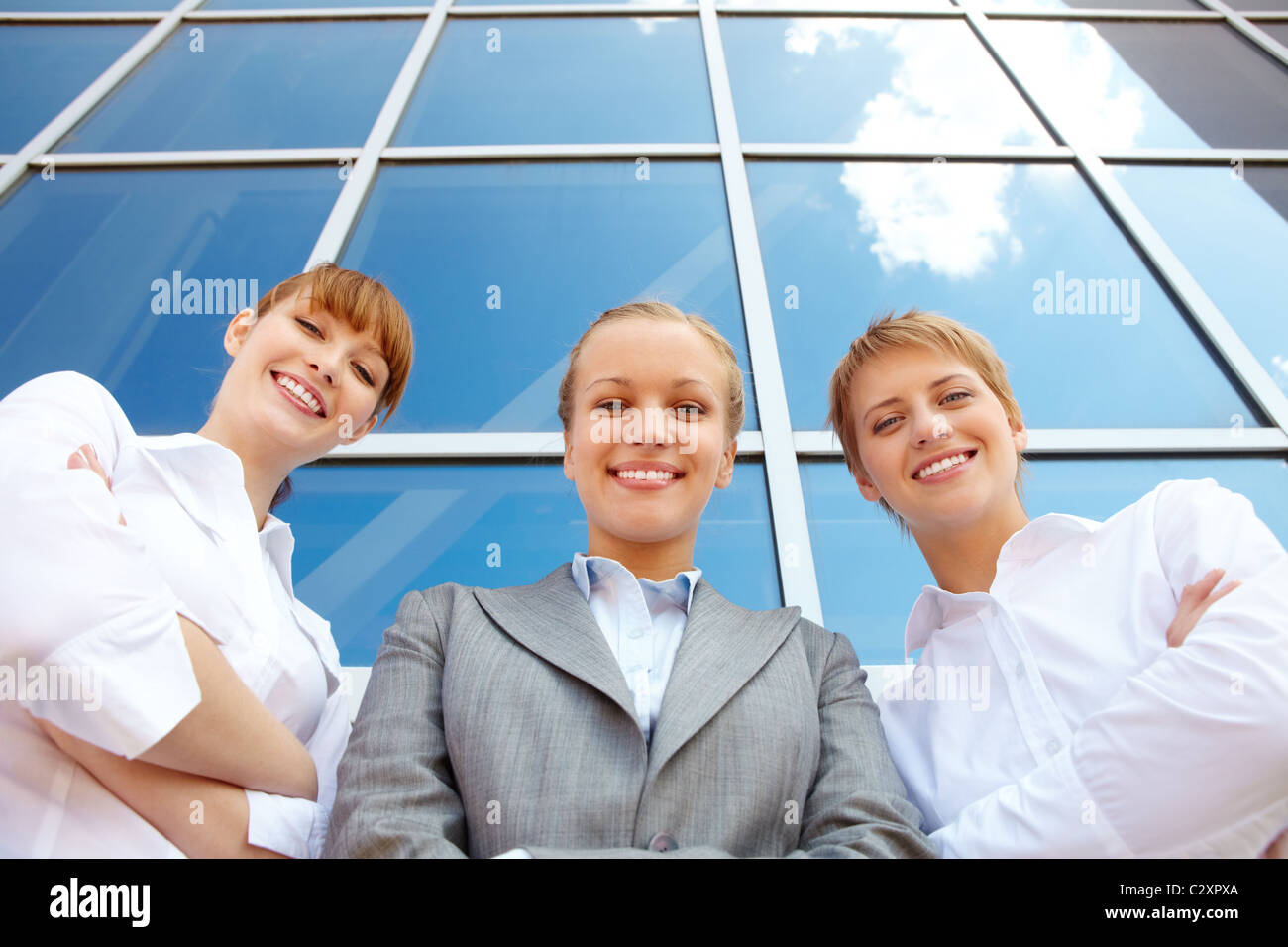 Below angle of three successful partners looking at camera with smiles ...