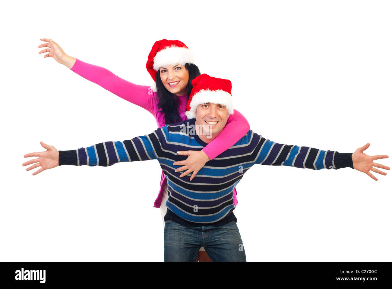 Cheerful couple wearing Santa hats and the man giving a piggy back ride ...