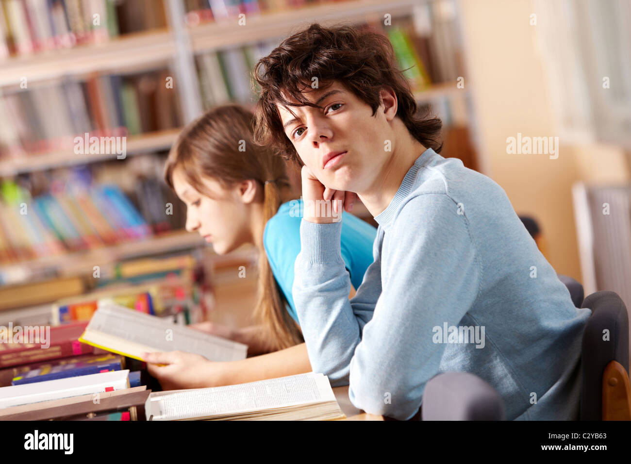 Portrait of pensive guy in library with his classmate reading on ...