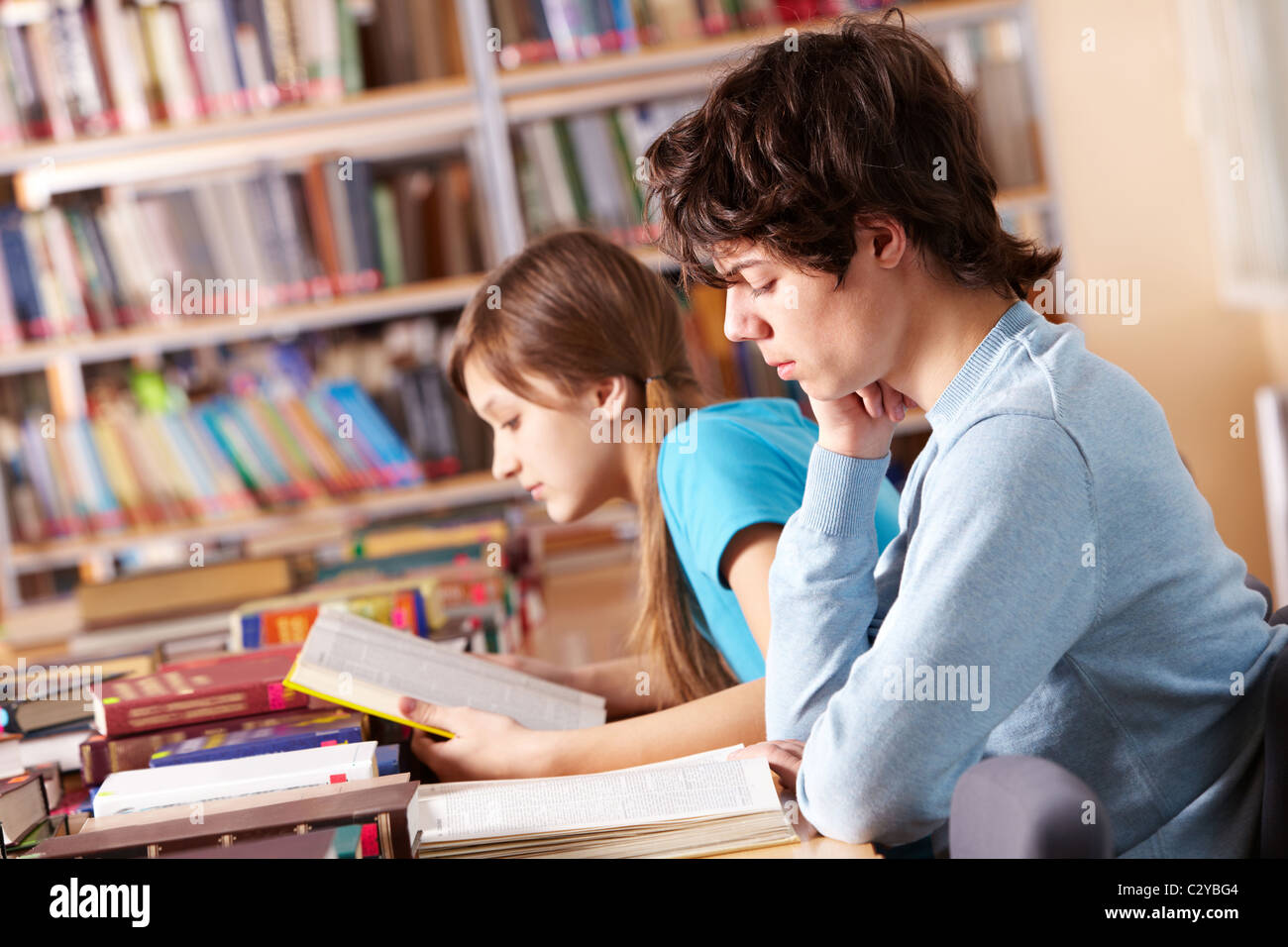 Portrait of serious guy reading book with his classmate on background ...