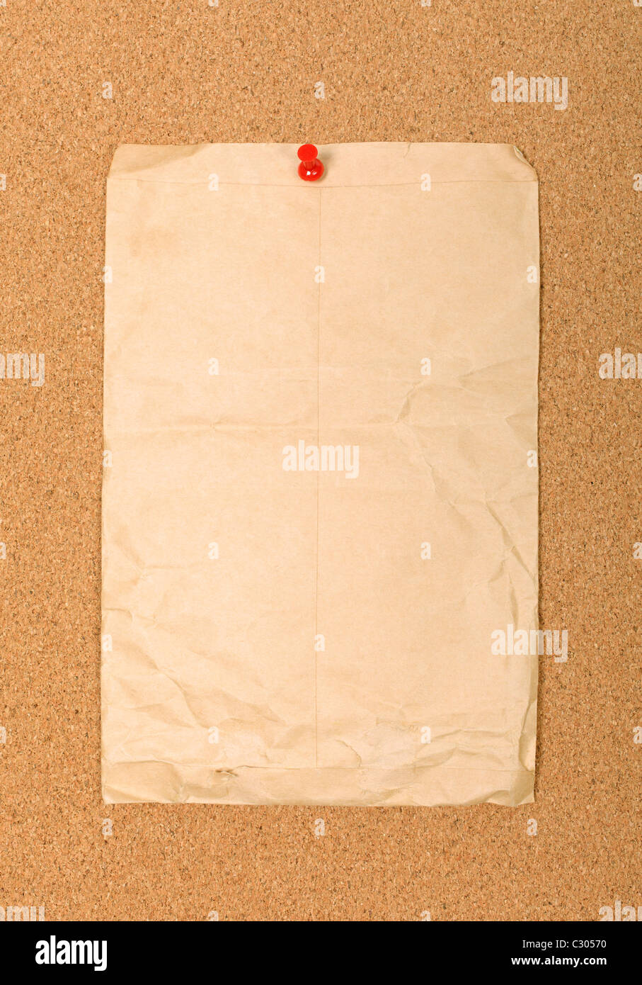 Wrinkled brown envelope attached to cork board with red pin. Empty ...