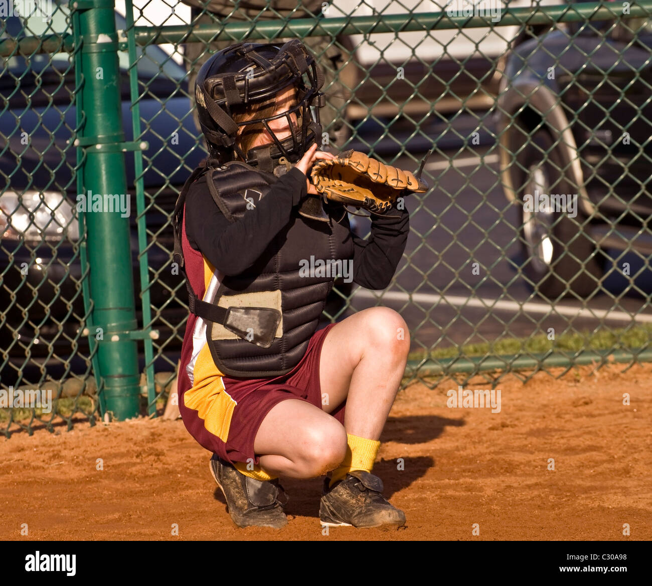 A young girl behind home plate watching intently ready to make a play ...