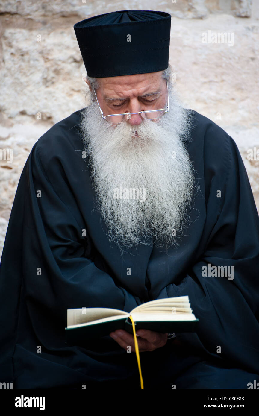 An Orthodox Christian priest with a long white beard sits reading a ...
