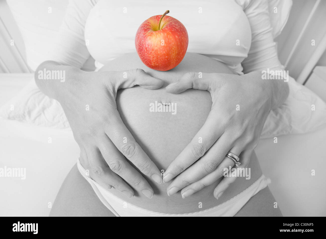 Smiling pregnant woman in high key mono with a red apple on her belly ...