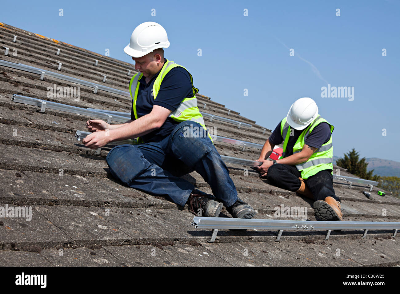 Two men fitting rails for solar pv panel attachment to house roof Wales ...