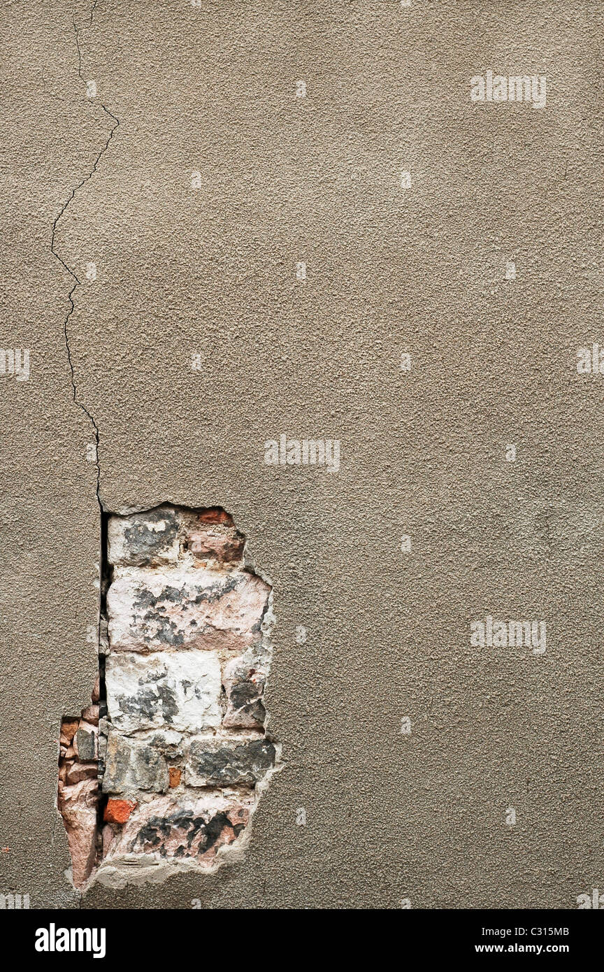 A concrete wall has cracked and crumbled to reveal the old bricks below ...