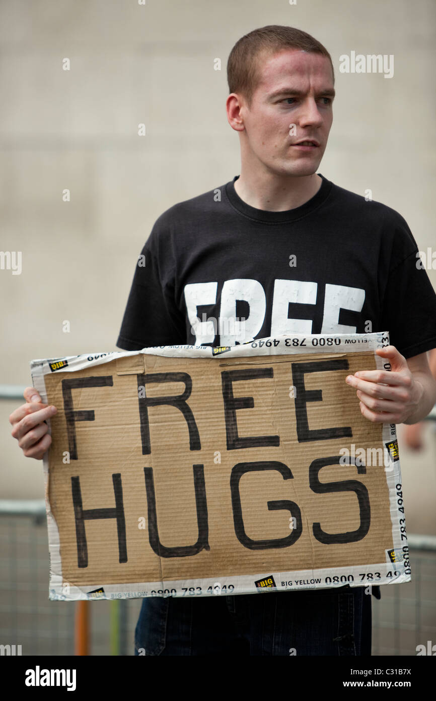 Portrait of a young man holding a Free Hugs sign in a public place ...