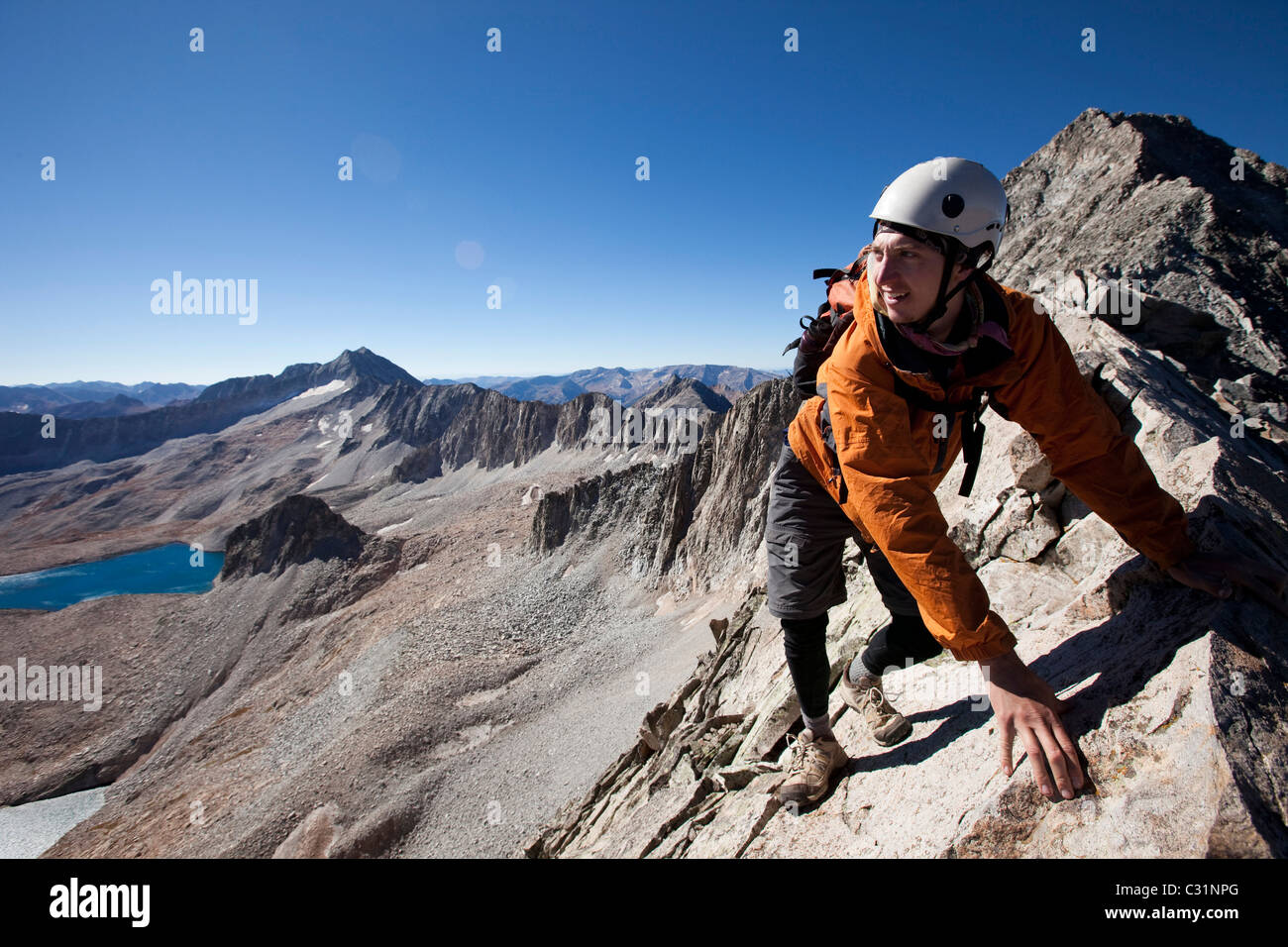 A young man crossing an exposed ridge line with the summit behind him ...