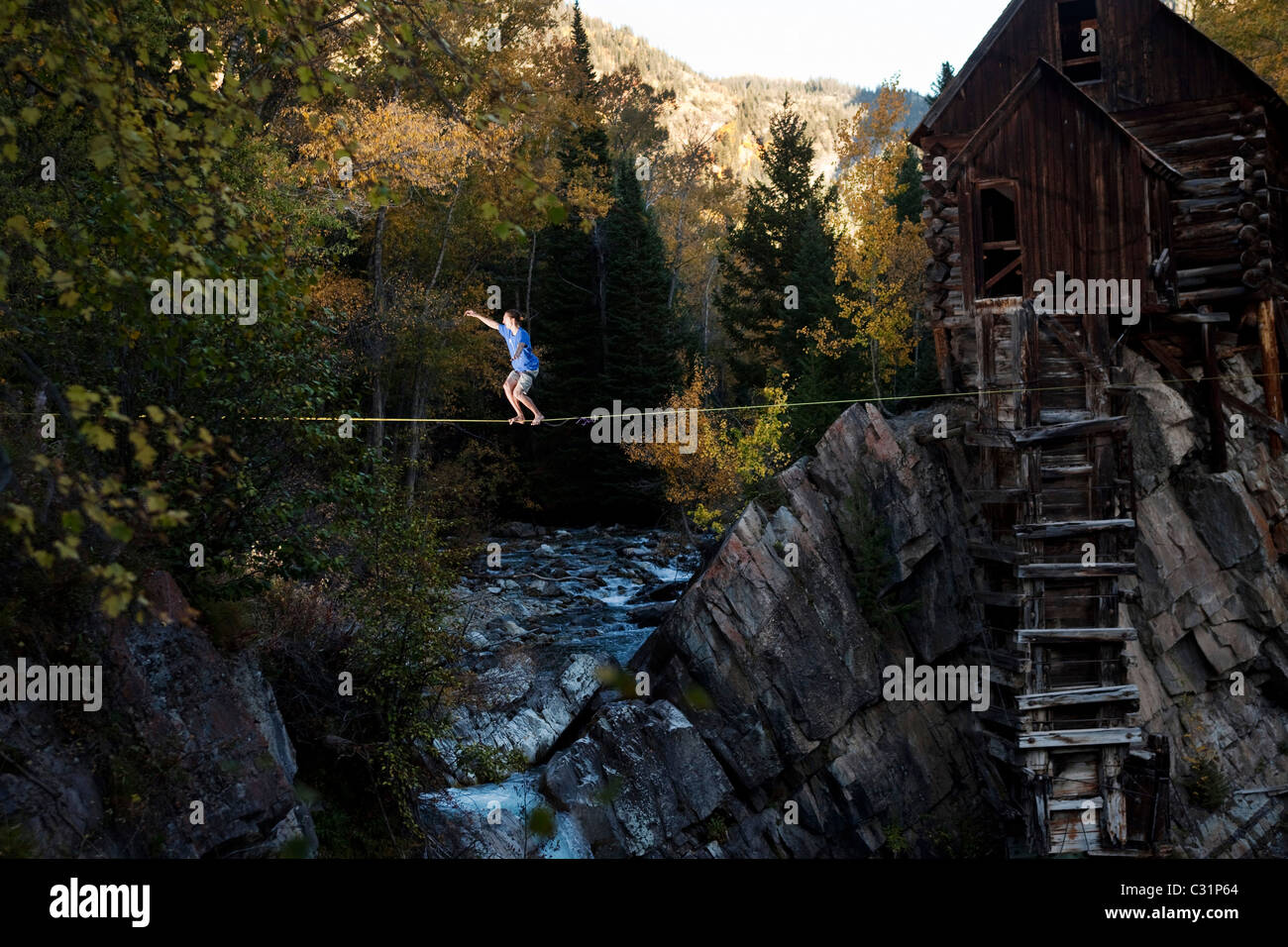 A young man walks a high line with glowing leaves and a raging river ...