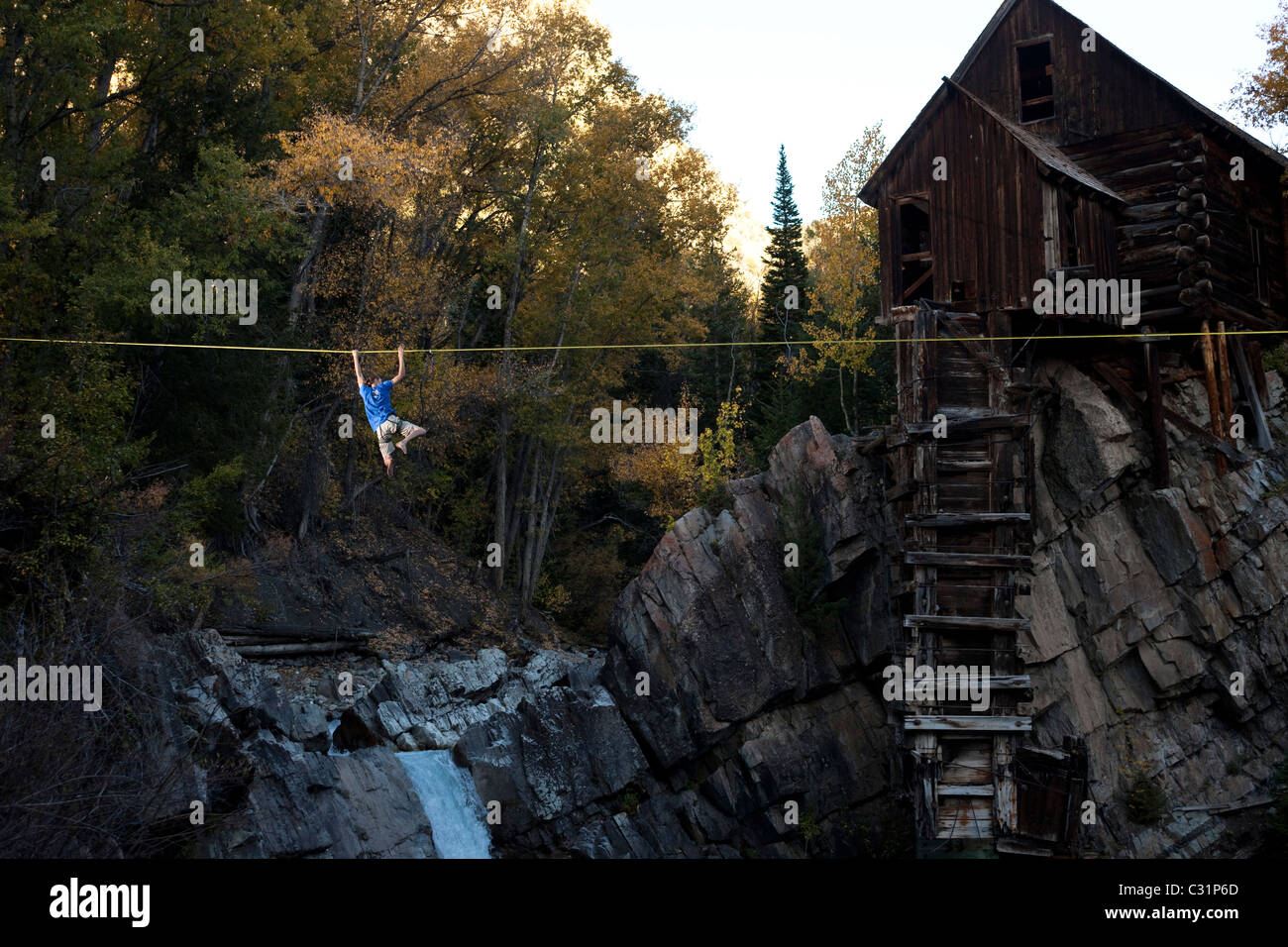 A young man swings a high line with glowing leaves and a raging river ...