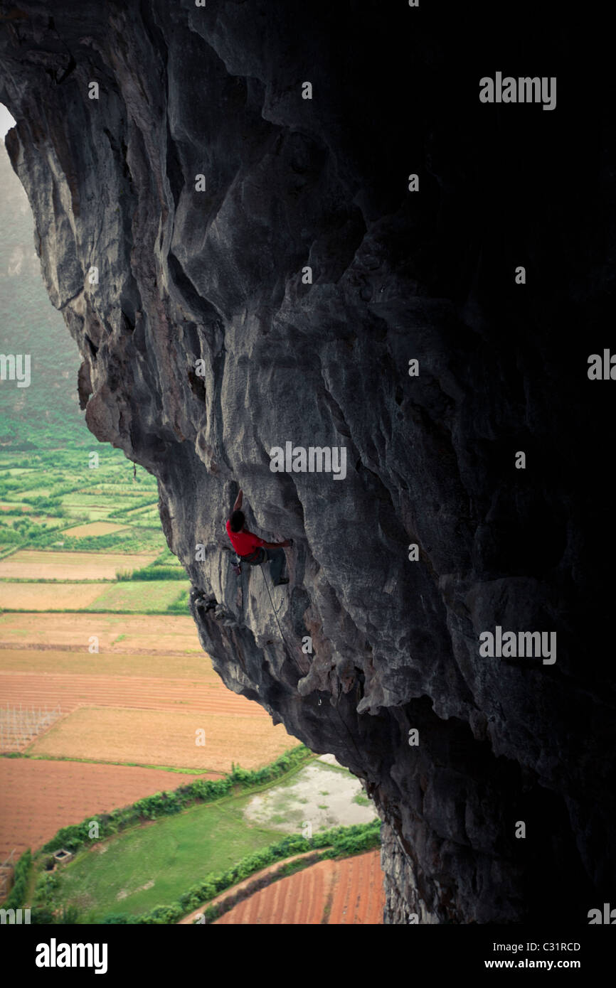 Male climber in a red shirt climbing an overhung cave wall in China ...