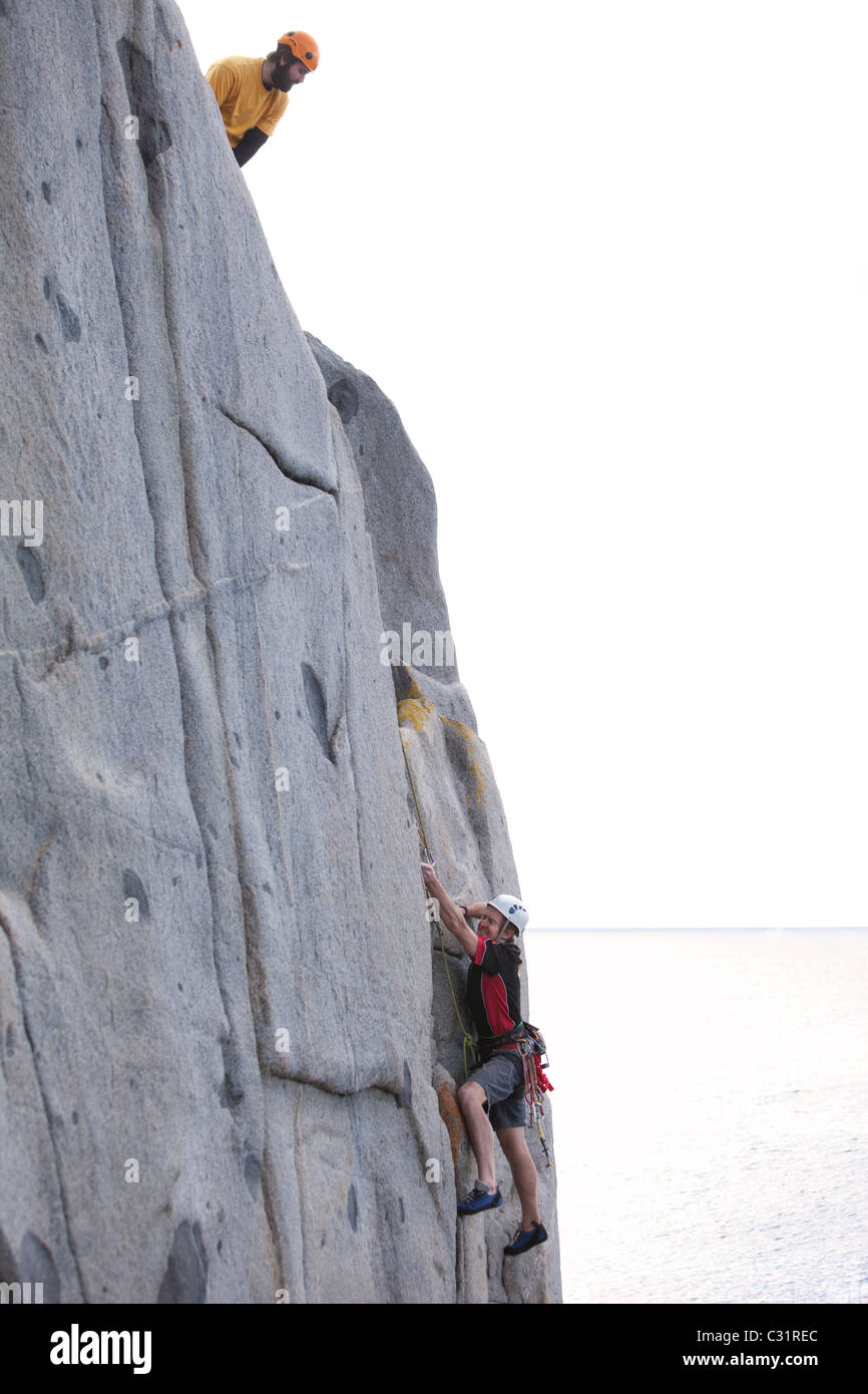 Male climber struggles with his gear while his belayer looks down from ...