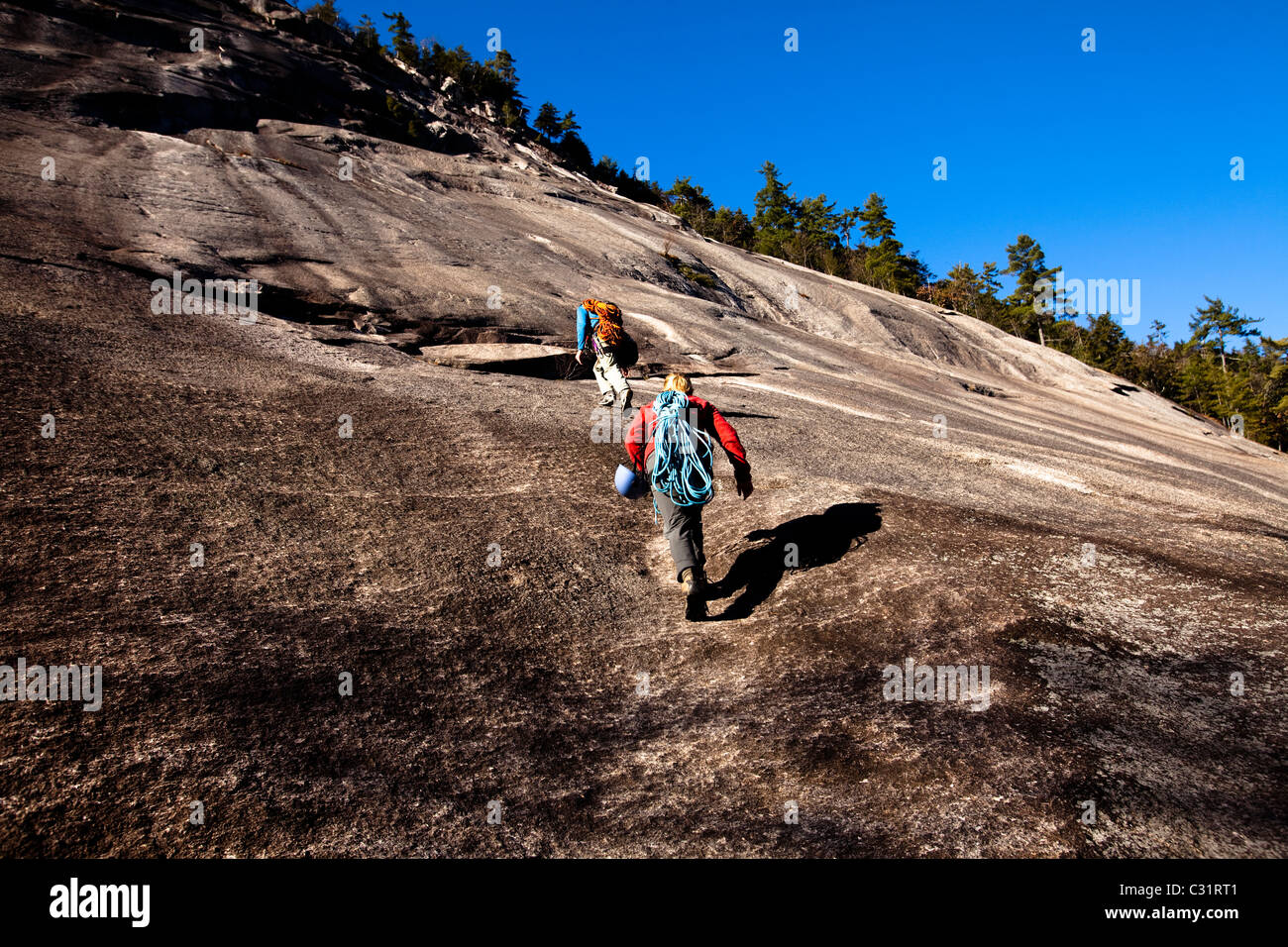 Two climbers carrying rope on their backs hike up a slab on White Horse ...