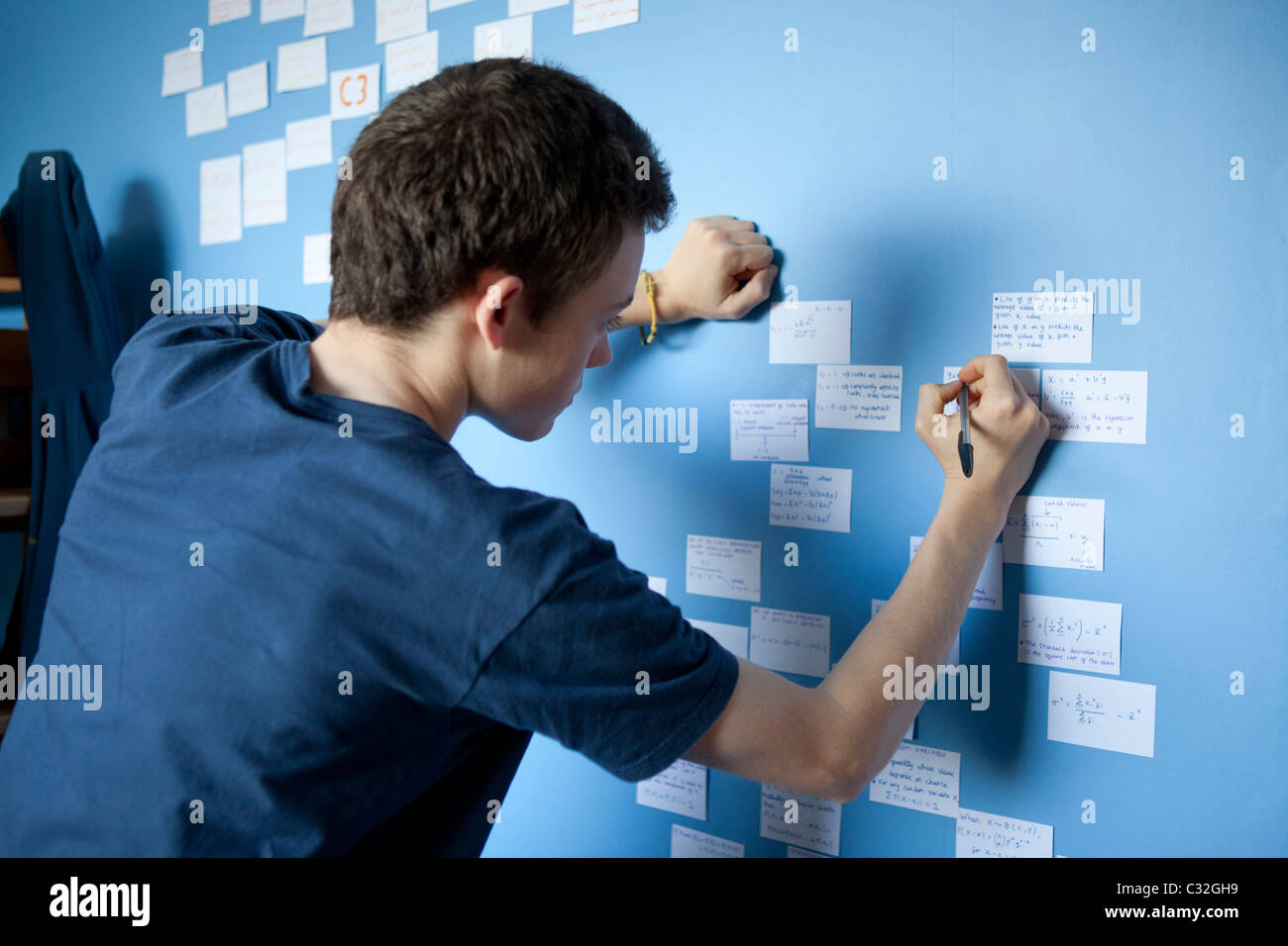 Teenage boy revising for Maths A Level with revision cards stuck on his ...