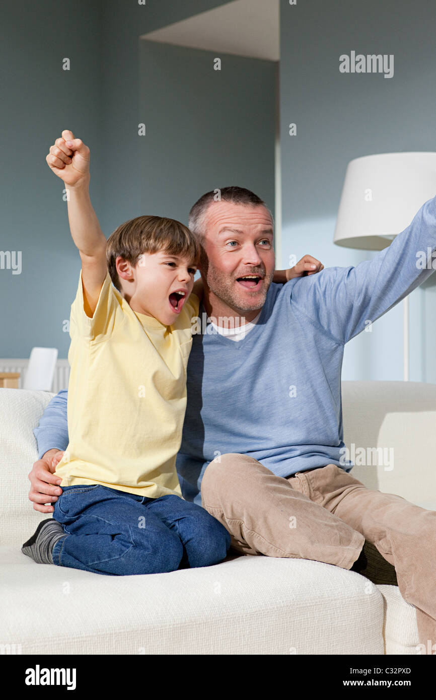 Father and son watching television cheering Stock Photo - Alamy