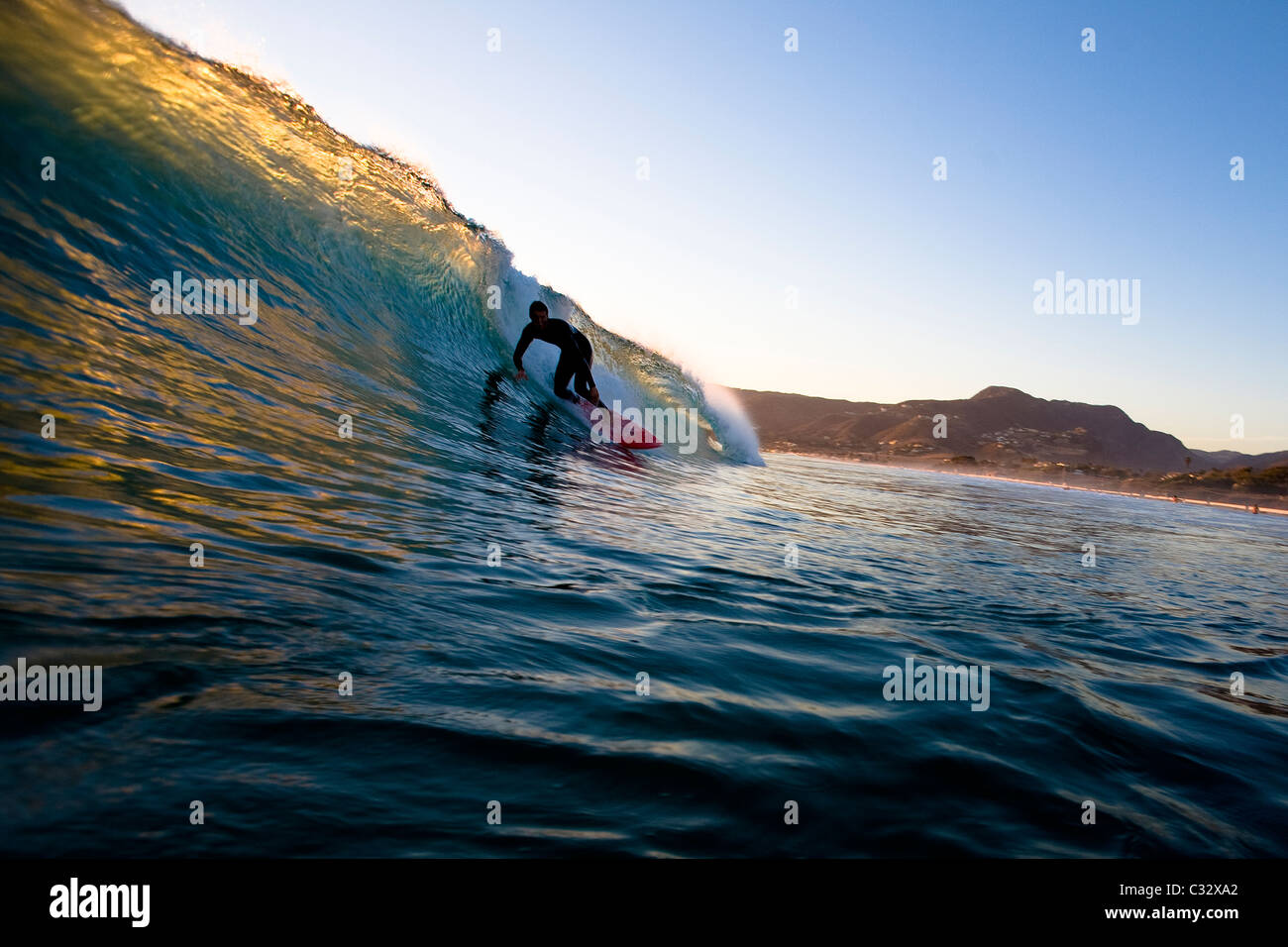 A surfer riding a red surfboard sets up for a barrel while surfing at ...