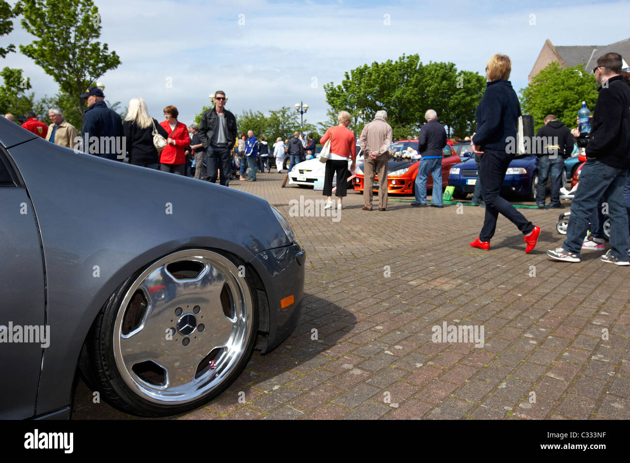 people walk past lowered car suspension and chrome wheels at a modified ...