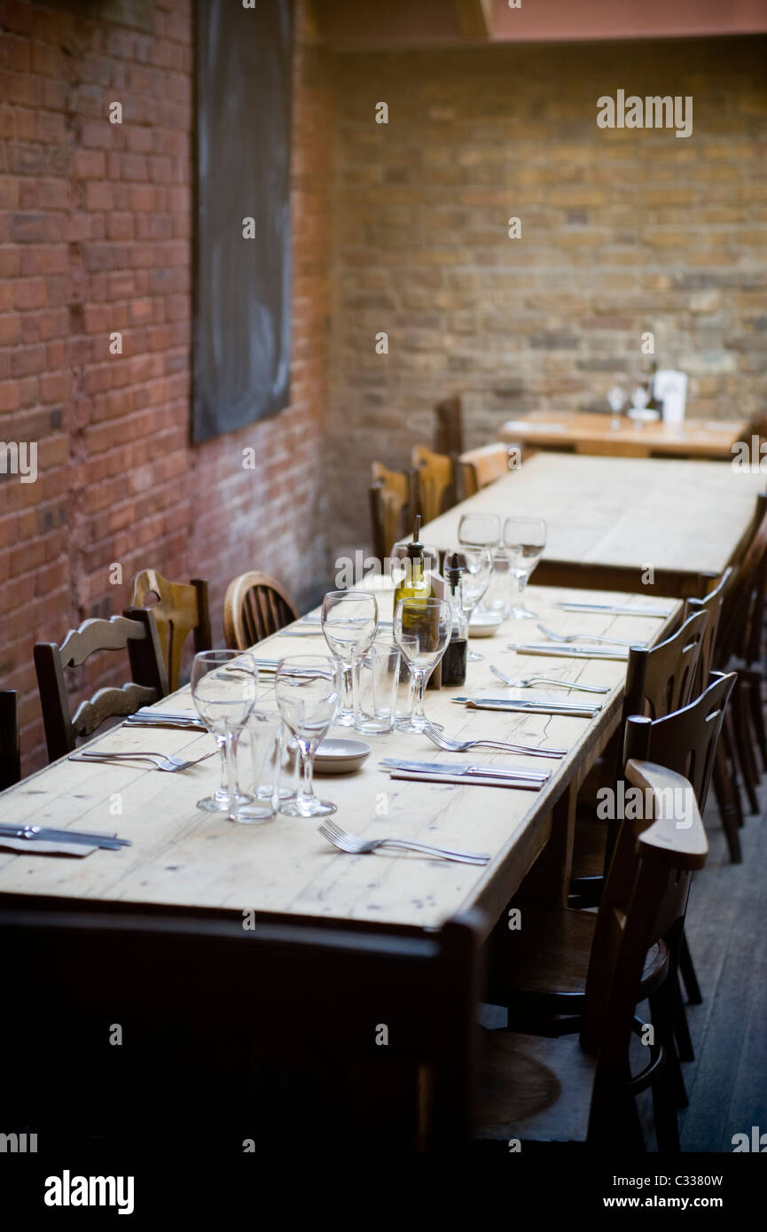 Wooden tables set in a restaurant with cutlery, glasses and condiments ...