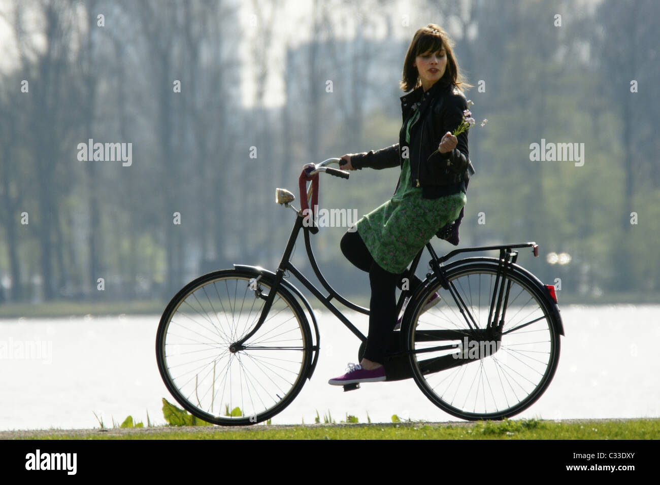 Young woman riding traditional Dutch bicycle holding bunch of flowers ...