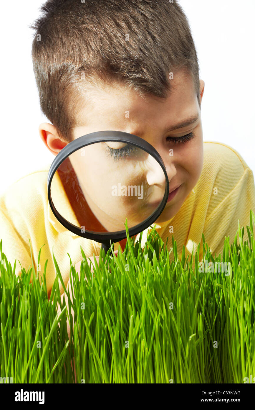 Photo of young boy looking at green grass through magnifying glass ...