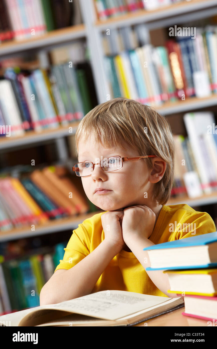 Portrait of clever boy thinking while reading book in library Stock ...