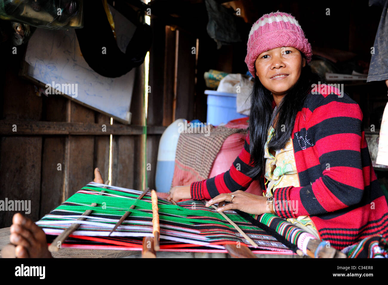 A woman weaves beautiful colors in her home to make cloth for garments ...