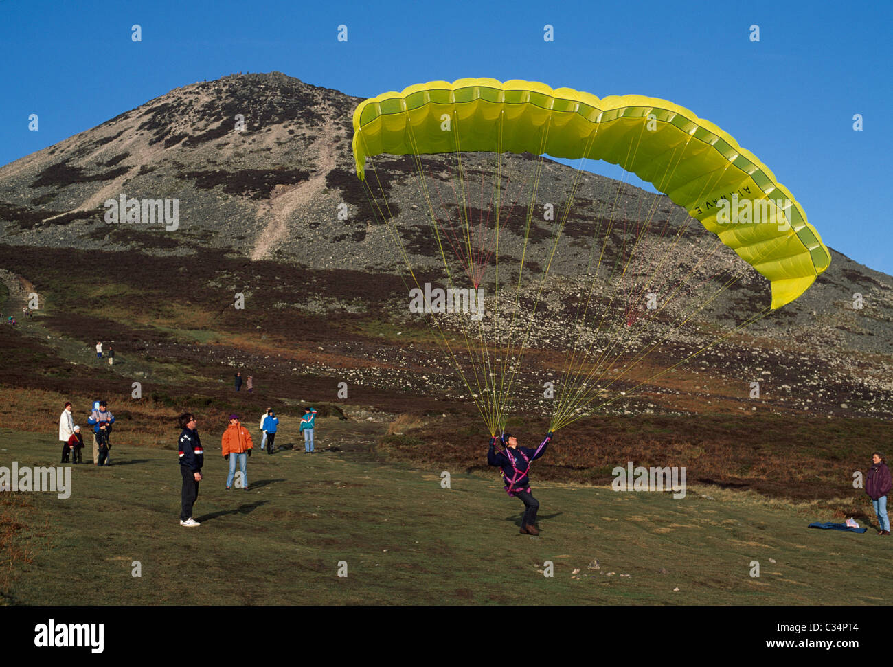 Yellow Parachuter Landing In Front Of Large Hill Stock Photo - Alamy