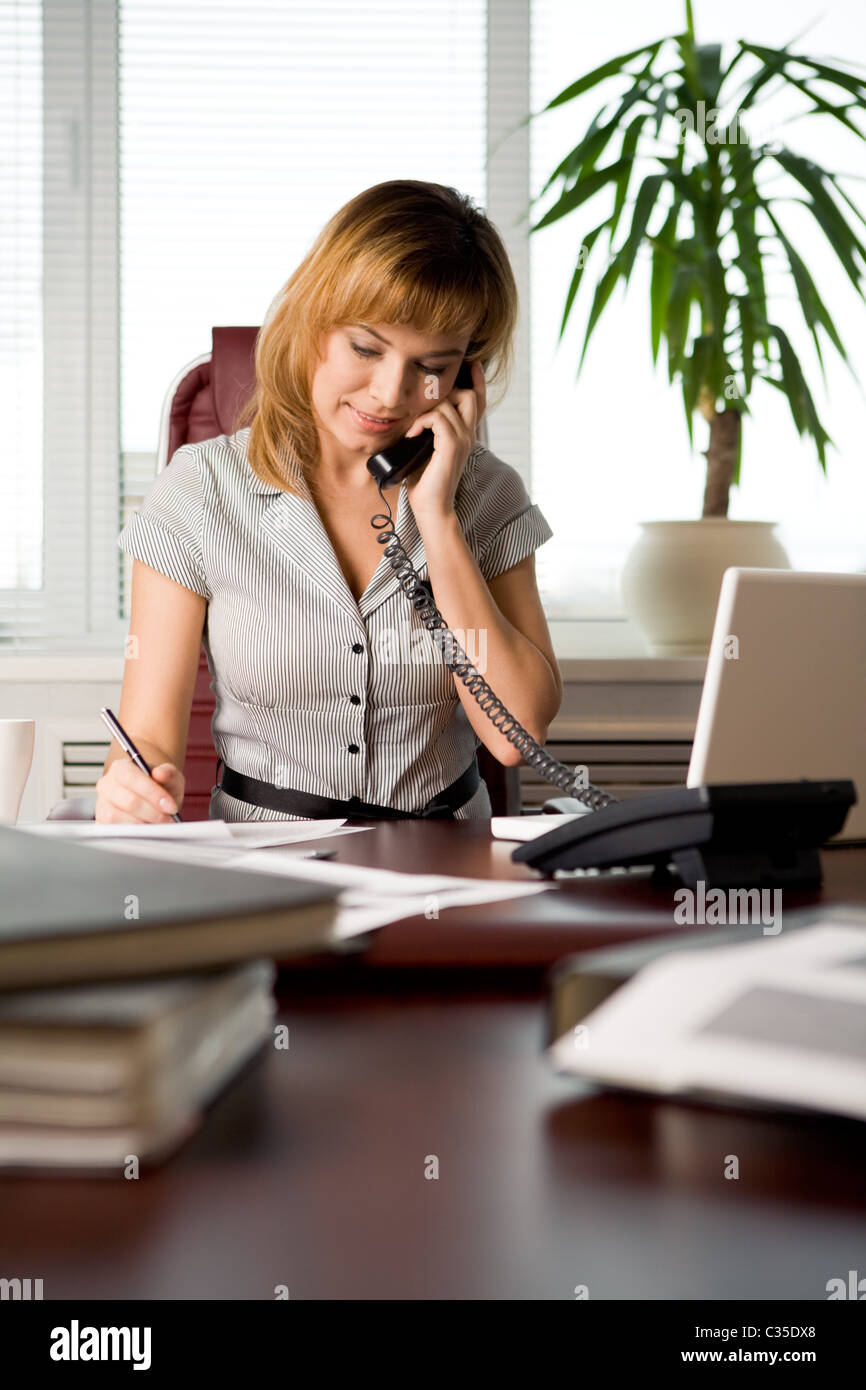 Busy secretary speaking on the phone and reading document in the office ...