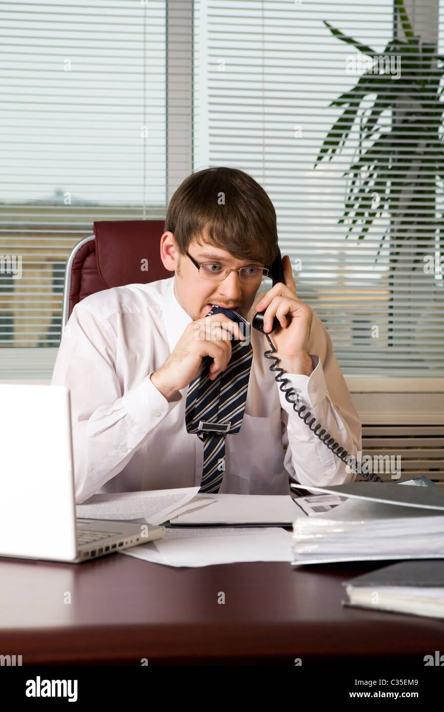 Portrait of scared boss with tie tip in mouth calling by the phone in ...