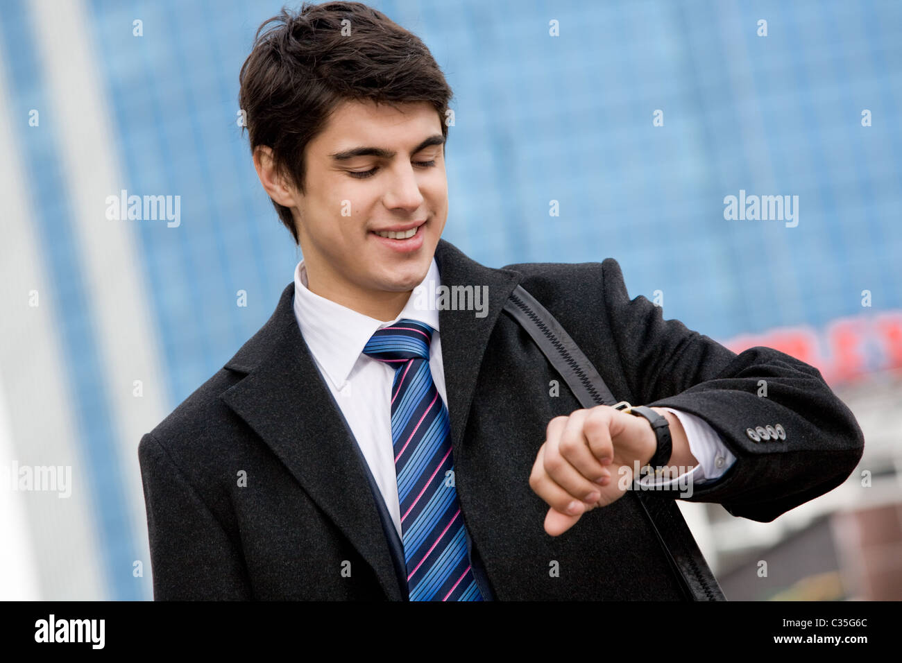 Photo of busy young man watching the time and smiling Stock Photo - Alamy