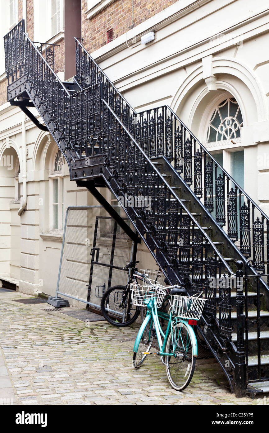 Green bicycle chained to a black, wrought iron staircase in a narrow ...