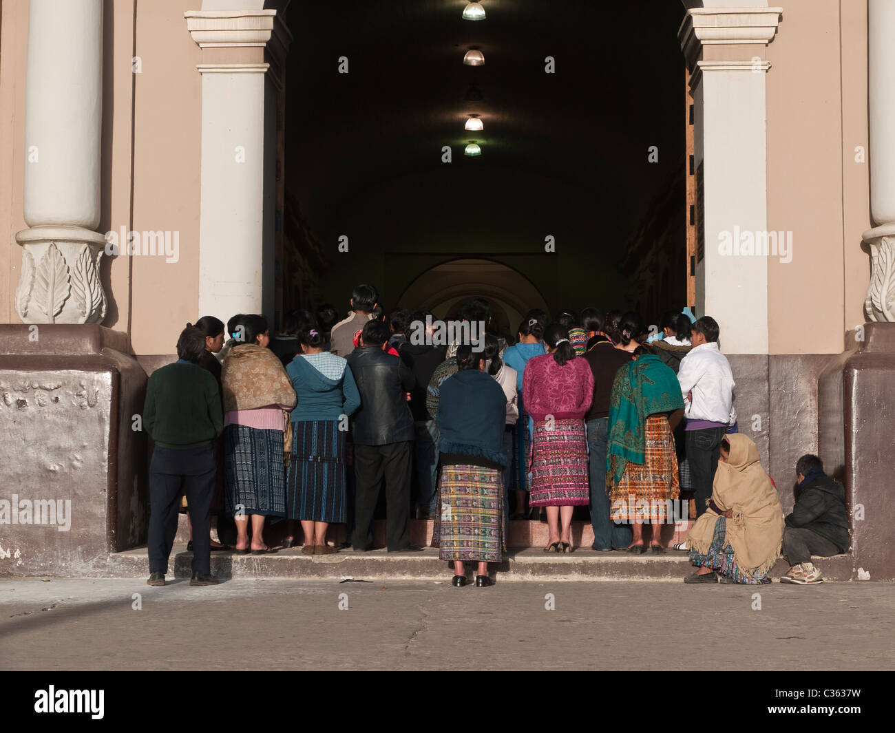 A crowd of worshipers stand in the doorway of the large colonial main ...