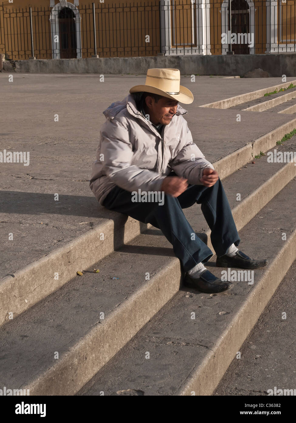 A middled aged Guatemalan man sits on steps of the large colonial ...
