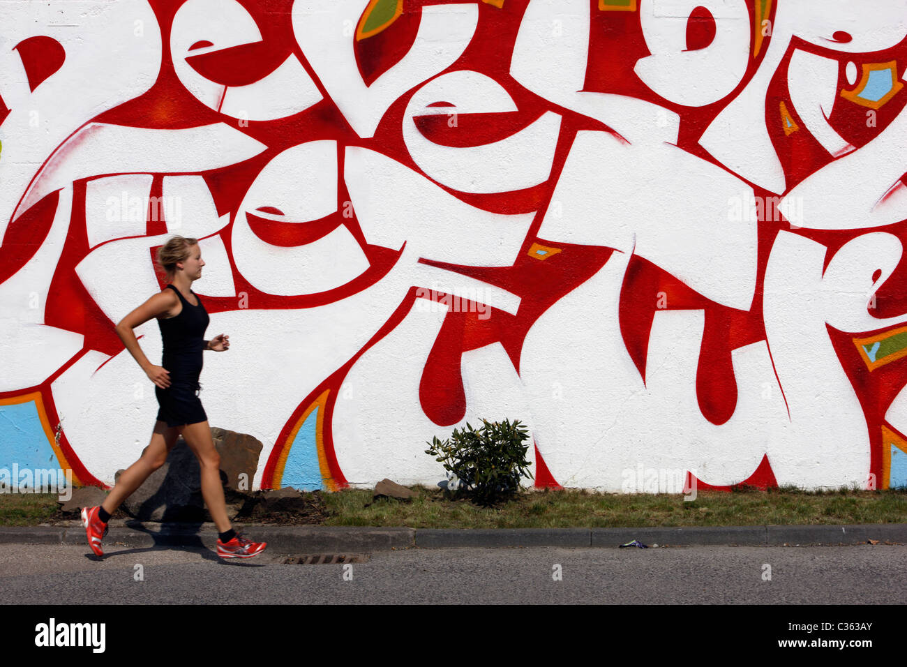 Female hobby runner. Jogging in a city, in front of a graffiti wall ...