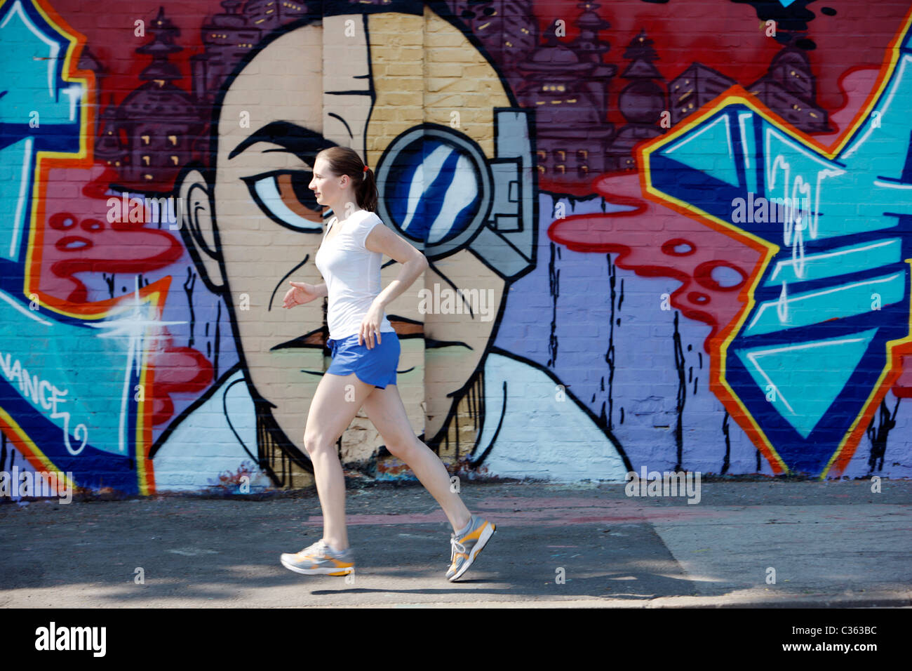 Female hobby runner. Jogging in a city, in front of a graffiti wall ...