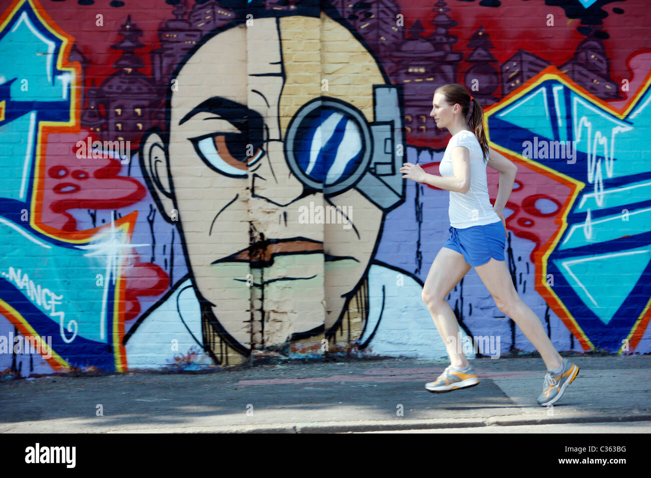 Female hobby runner. Jogging in a city, in front of a graffiti wall ...