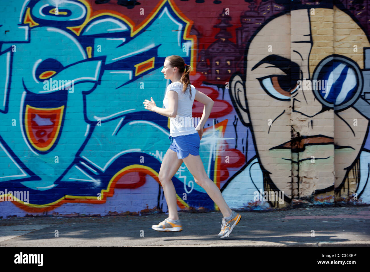 Female hobby runner. Jogging in a city, in front of a graffiti wall ...