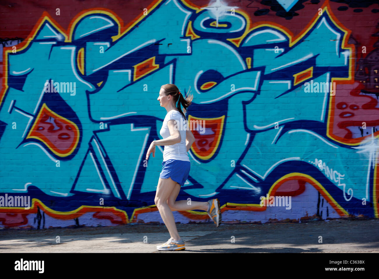 Female hobby runner. Jogging in a city, in front of a graffiti wall ...