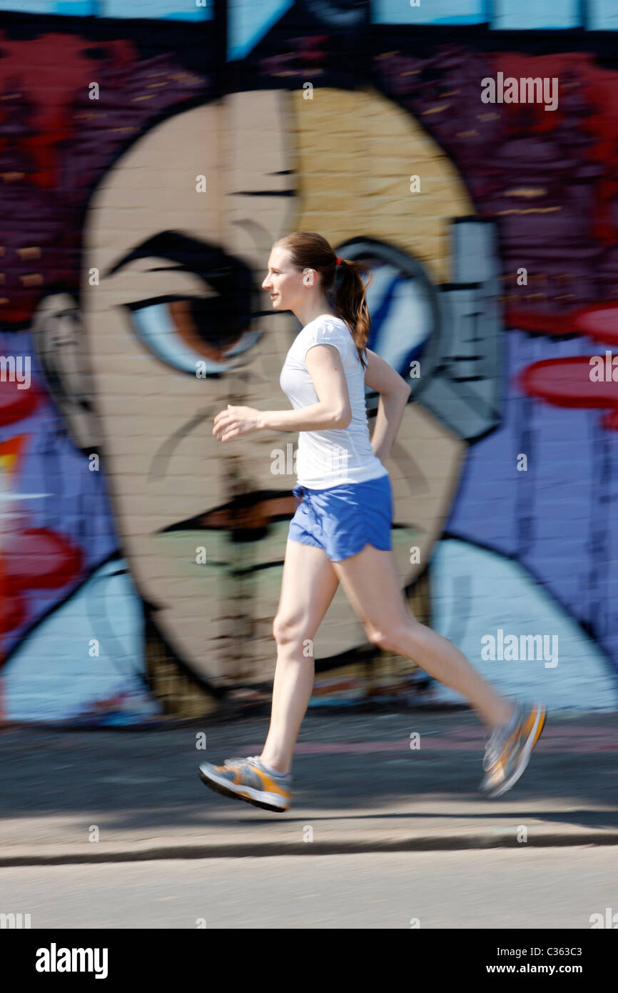 Female hobby runner. Jogging in a city, in front of a graffiti wall ...