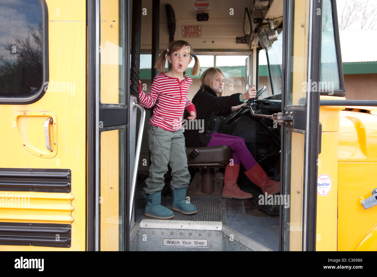 Girl pretending to drive a school bus while her sister looks out the ...