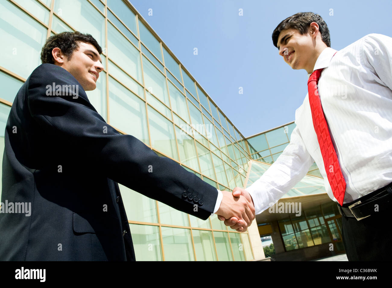 Photo of happy co-workers handshaking outdoors at background of modern ...